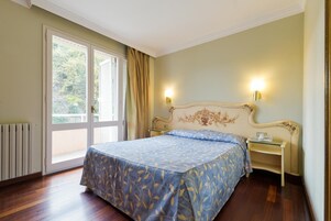 Quarto de hotel com uma cama grande, uma mesa de cabeceira, uma luminária e vista para o exterior por uma porta deslizante.