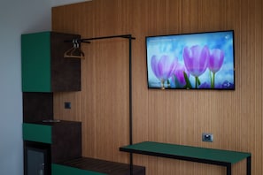 Quarto moderno com parede revestida em madeira, televisão montada exibindo flores, um banco verde e um porta-roupas.