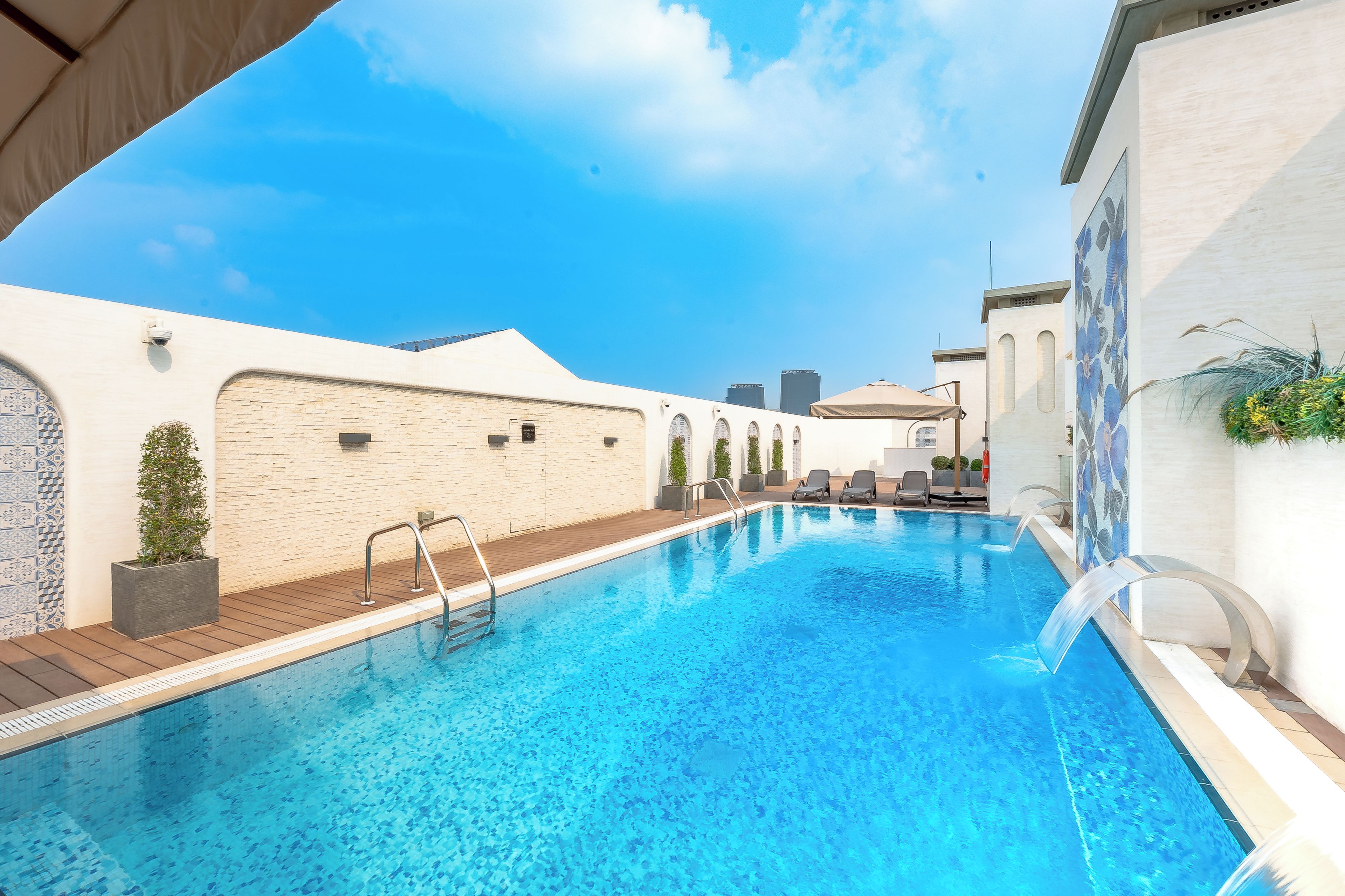 Uma piscina com deck de madeira, espreguiçadeiras e um céu azul cristalino.