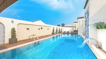 Uma piscina com deck de madeira, espreguiçadeiras e um céu azul cristalino.