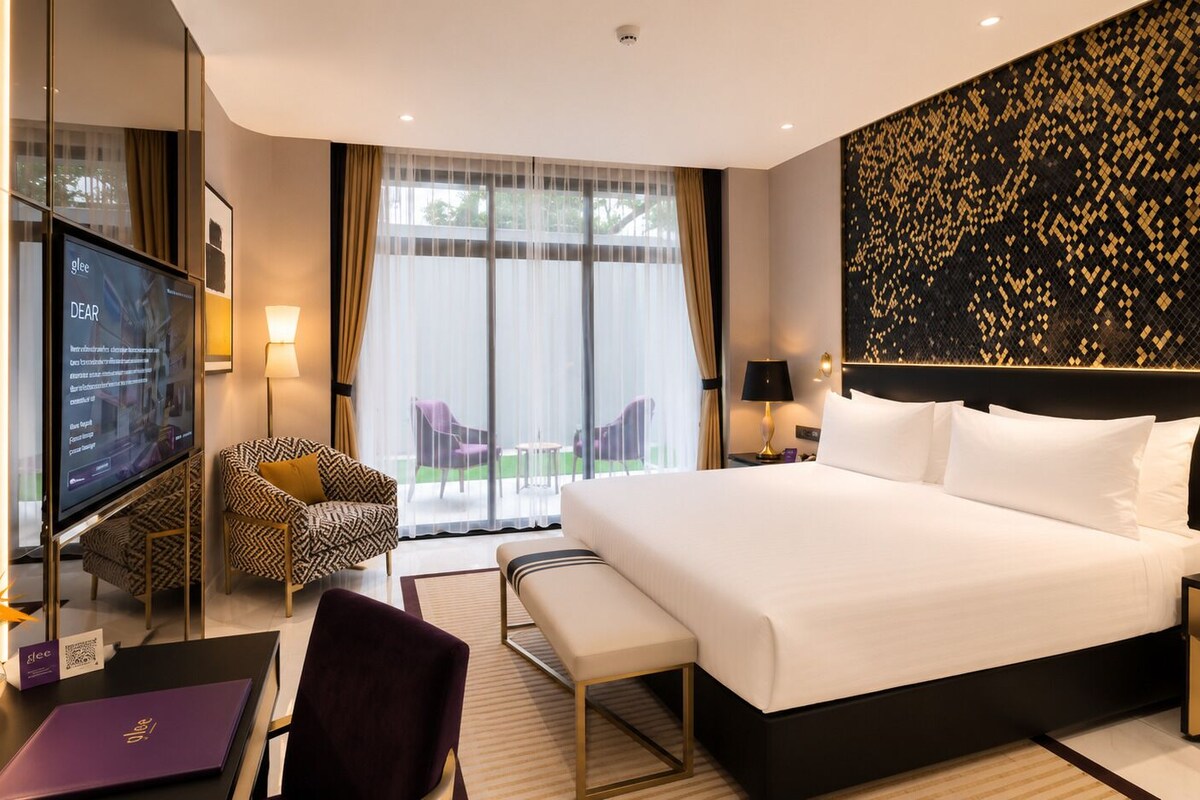 Quarto de hotel com uma cama grande, uma escrivaninha com computador, uma cadeira, televisão e vista para o exterior.