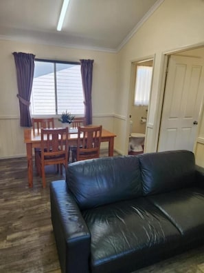 Um quarto com uma mesa de jantar e cadeiras, um sofá de couro preto e uma porta que dá para outro cômodo.