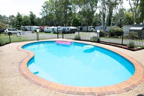 Piscina com borda de tijolos, cercada por uma grade, e trailers ao fundo.