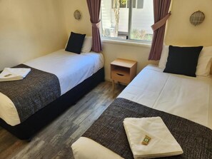 Quarto com duas camas, uma mesinha de cabeceira de madeira e uma janela com cortinas.
