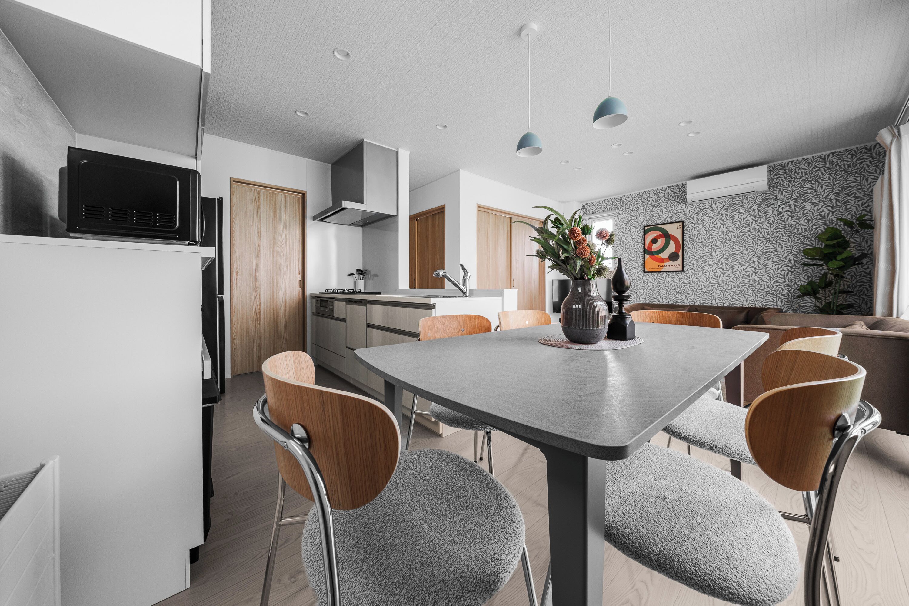 Cozinha moderna com área de refeições, com ilha central, cadeiras de madeira e iluminação pendente.