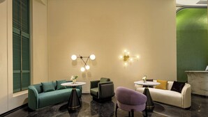 Uma área de estar moderna com um sofá verde, um sofá branco e uma poltrona roxa, além de duas mesas redondas e uma luminária decorativa.