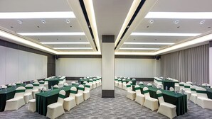 Uma sala de conferências com mesas e cadeiras dispostas em fileiras, piso coberto por carpete e iluminação embutida no teto.