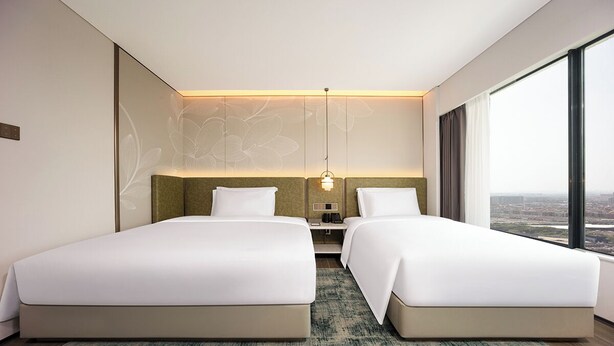 Quarto de hotel moderno com duas camas, uma mesa de cabeceira e vista para a cidade.