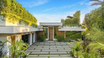 Uma casa moderna com entrada central, cercada por um jardim com diversas plantas e um caminho pavimentado.
