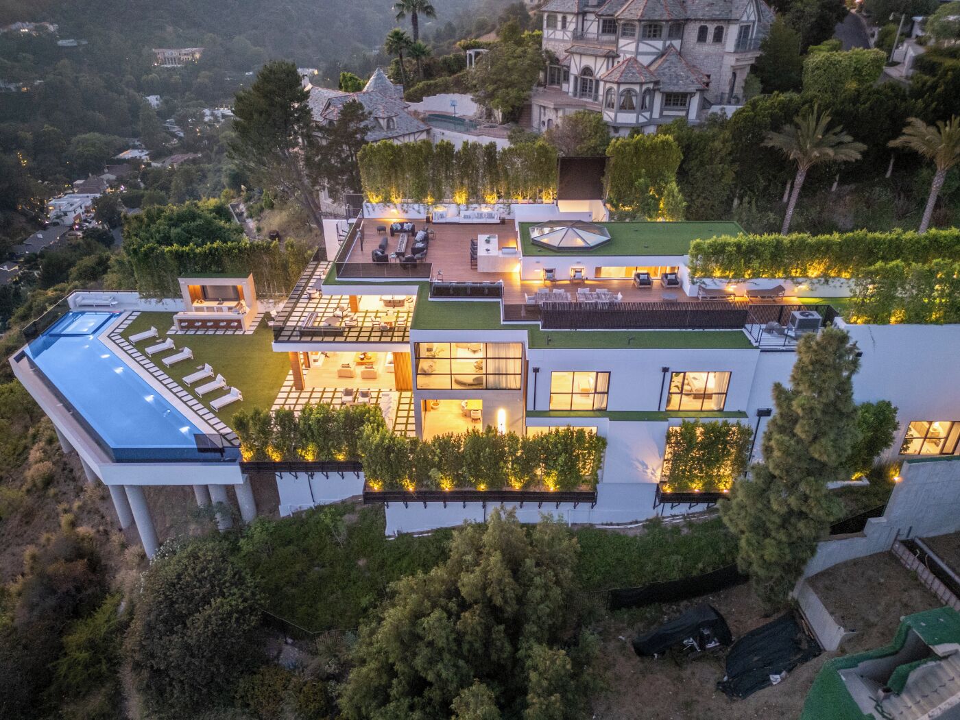 Uma casa moderna de vários andares com piscina no terraço, áreas de estar ao ar livre e um jardim bem cuidado.