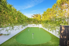 Um campo de minigolfe com grama sintética verde, rodeado por vegetação exuberante e árvores.