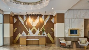 Uma área de recepção de hotel com design moderno, incluindo um balcão de atendimento, espaço para sentar e um lustre grande.