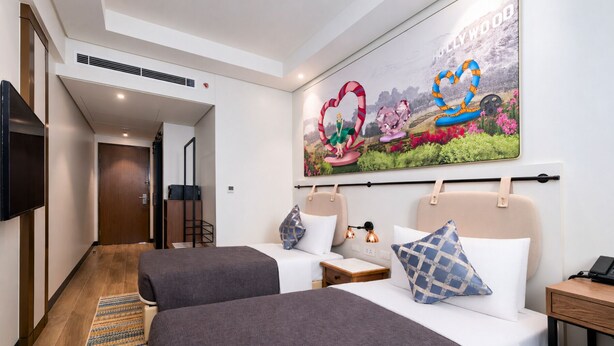 A hotel room with two beds, a flat-screen TV, a painting, and a wooden floor.