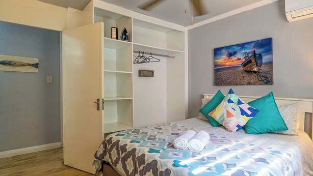 Um quarto com cama, guarda-roupa, um quadro e ventoinha no teto.