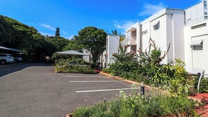 Um estacionamento com galeria coberta, anexo a um edifício com fachada branca e sacadas.