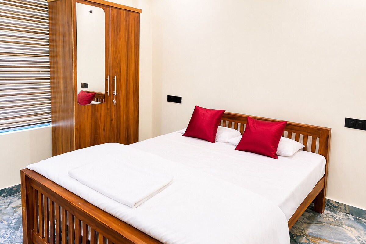 Quarto de hotel com estrutura de cama de madeira, roupa de cama branca e almofadas vermelhas.