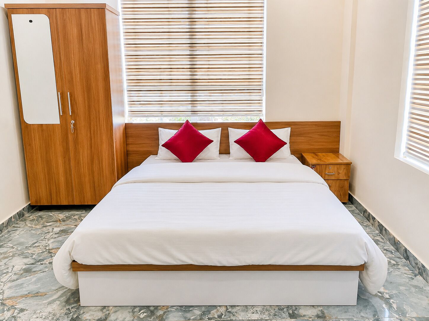 Quarto de hotel com uma cama, um guarda-roupa de madeira, uma mesa de cabeceira e uma janela com persianas.