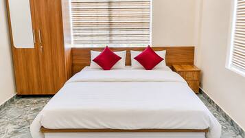 Quarto de hotel com uma cama, um guarda-roupa de madeira, uma mesa de cabeceira e uma janela com persianas.