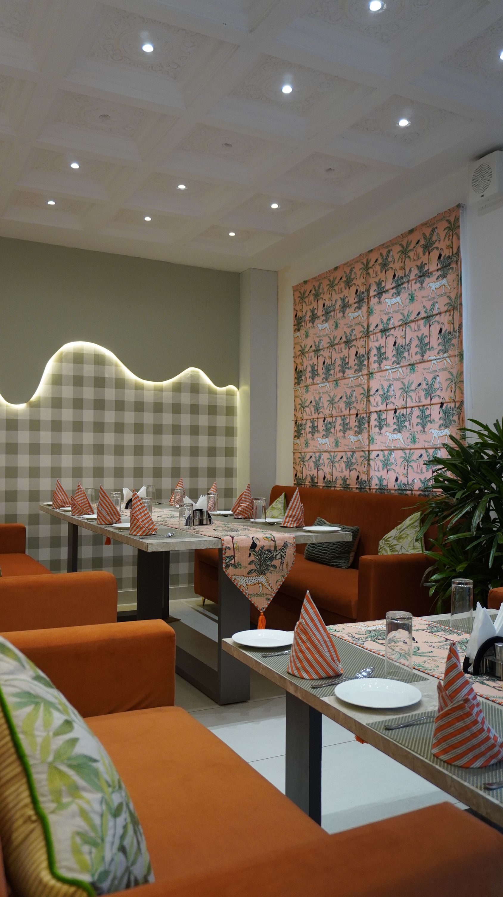 Restaurante com paredes quadriculadas, tapeçaria estampada e assentos estofados em laranja.