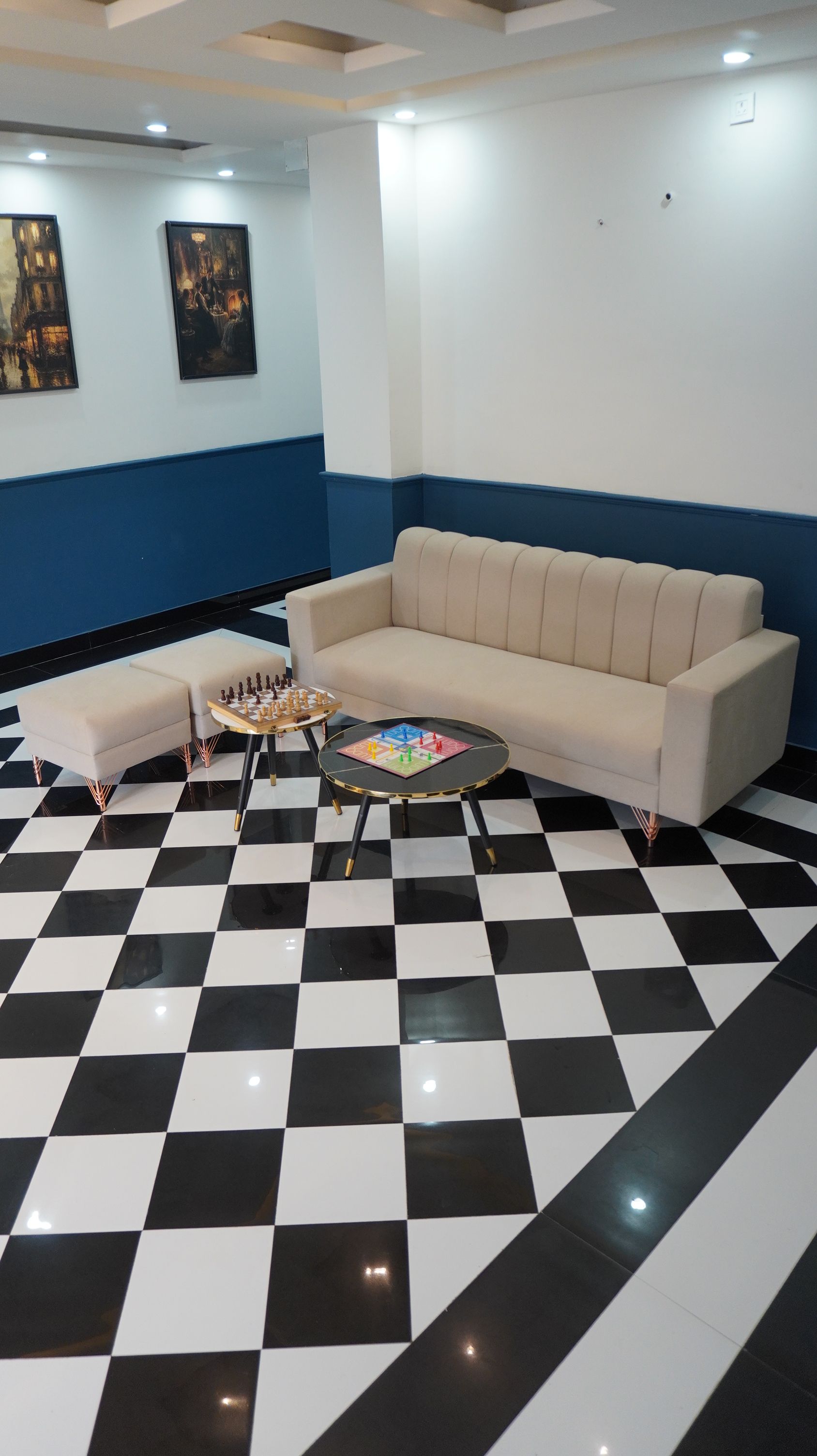 Um hall com piso xadrez, um sofá, uma mesa de centro e dois pufes.