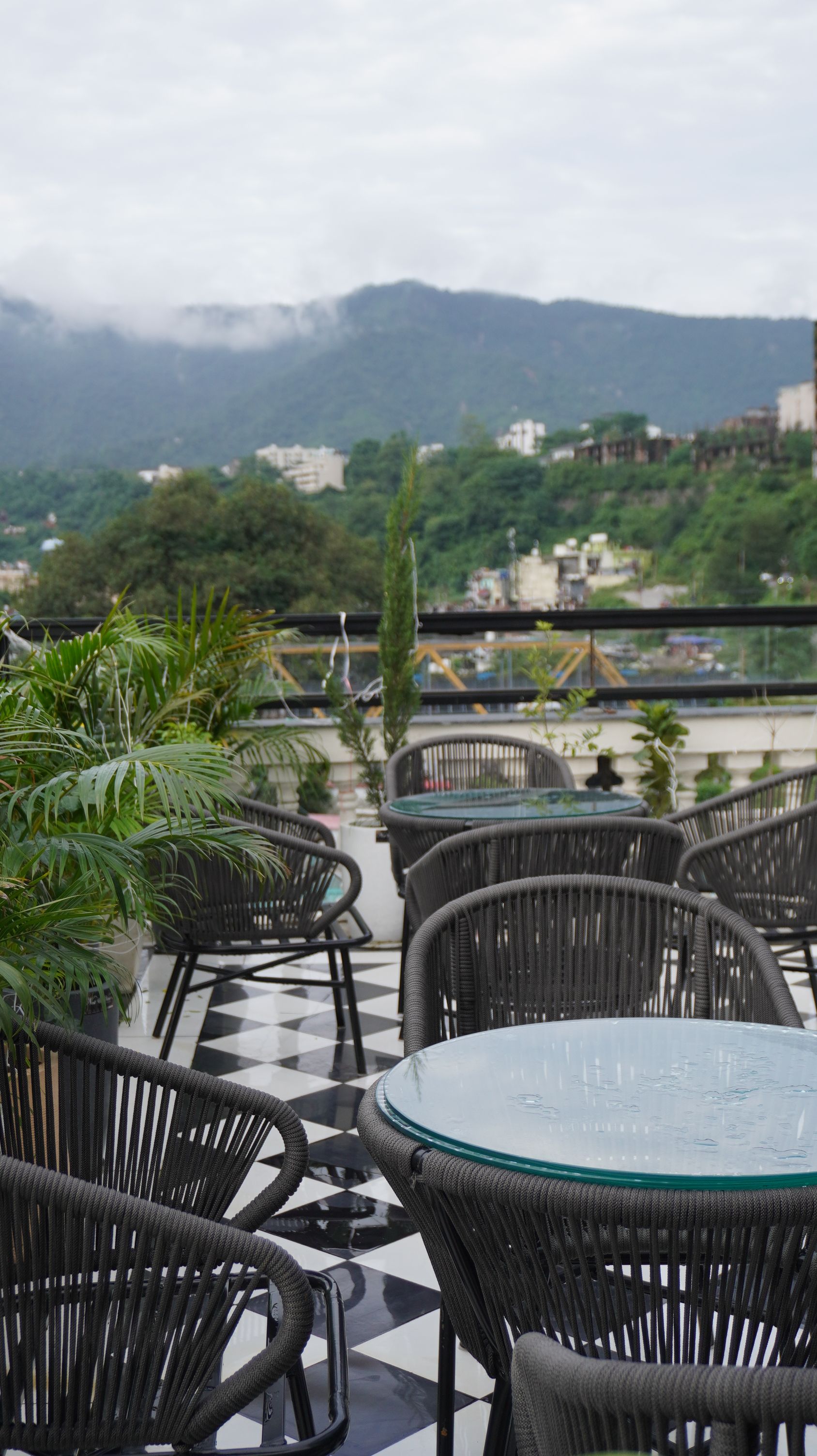 Terraço com cadeiras de vime e uma mesa de vidro, com vista para uma paisagem montanhosa.