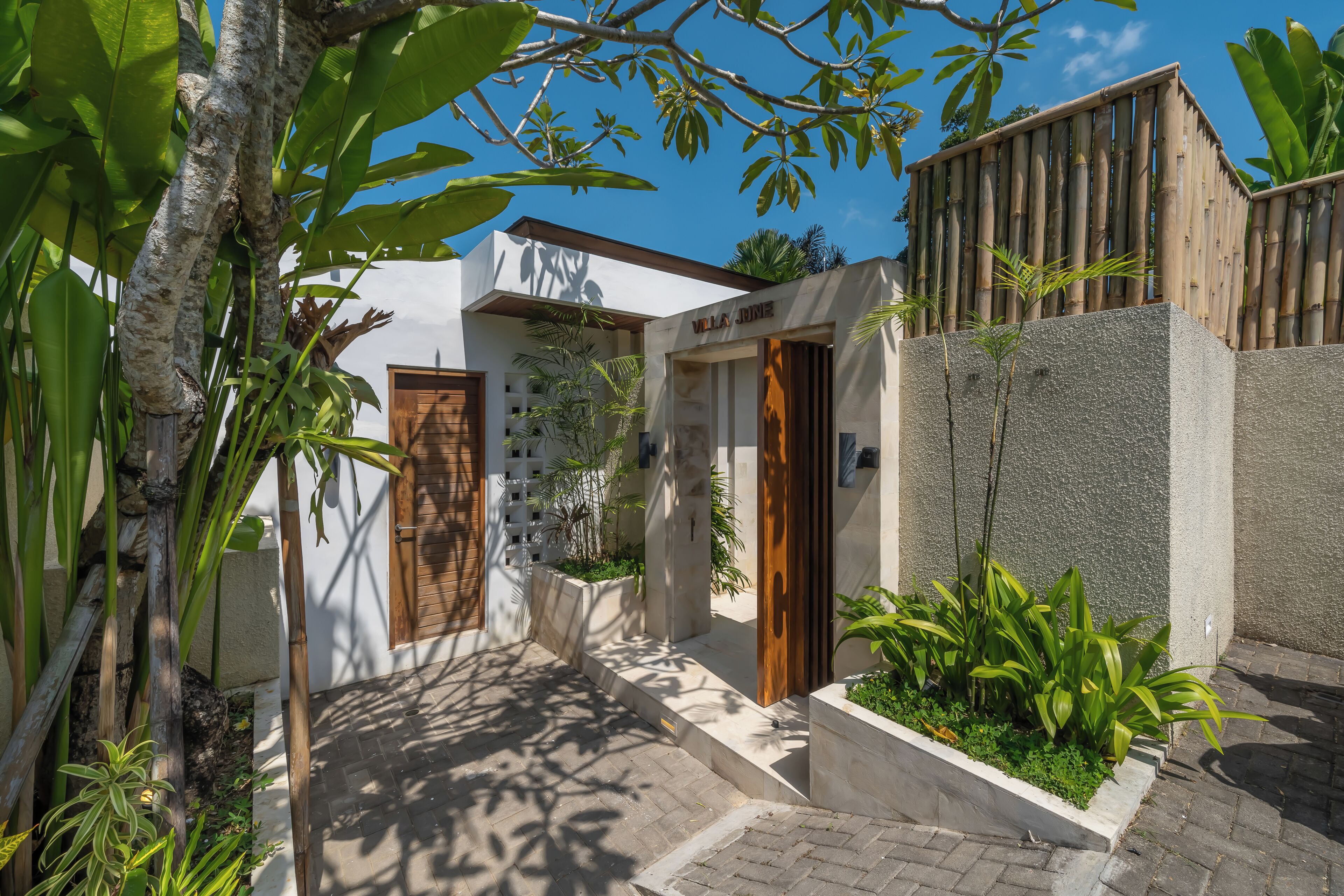 Uma villa moderna com porta de madeira, parede branca com janela e uma placa com o nome 'VILLA JUNE'.