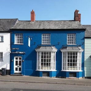 Um edifício de dois andares com fachada azul, uma porta branca e uma placa com a inscrição 'Mansion Street'.