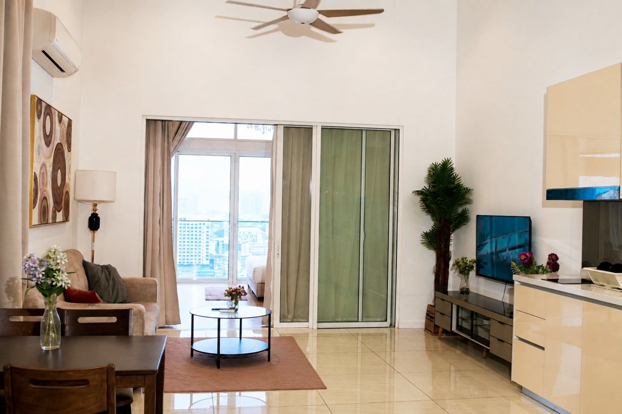 Uma sala de estar moderna com sofá, mesa de centro e televisão. Há uma porta de vidro deslizante que dá para uma varanda.