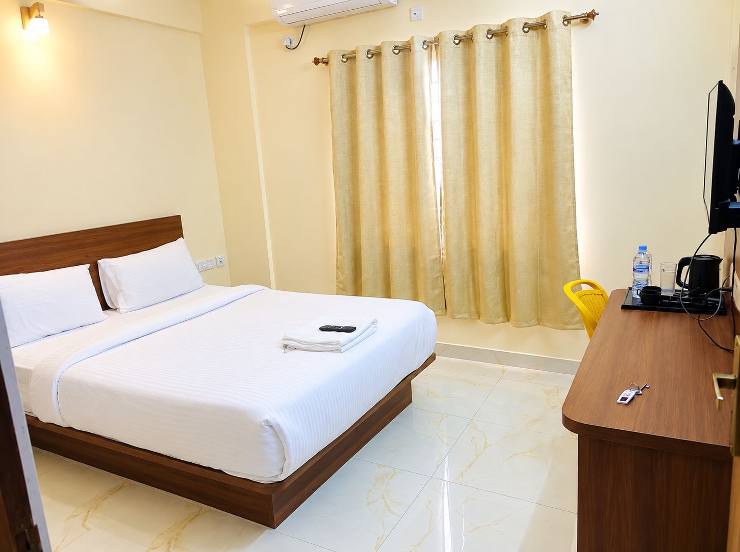 Quarto de hotel com cama, secretária com chaleira, cadeira e cortina.