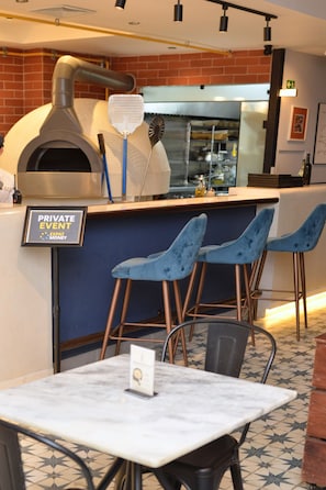 Interior de restaurante com parede de tijolos, forno a pizza, banquetas de bar e placa indicando evento privado.