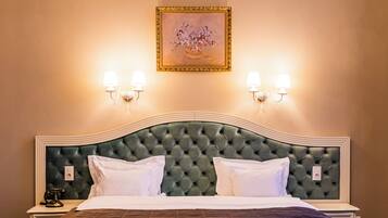 Quarto de hotel com cabeceira estofada, duas luminárias de apoio, uma obra de arte emoldurada acima da cabeceira e cama com roupa de cama branca.
