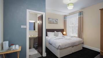Quarto de hotel com uma cama, uma mesa de cabeceira com abajur, uma janela com cortinas e um banheiro visível através de uma porta aberta.