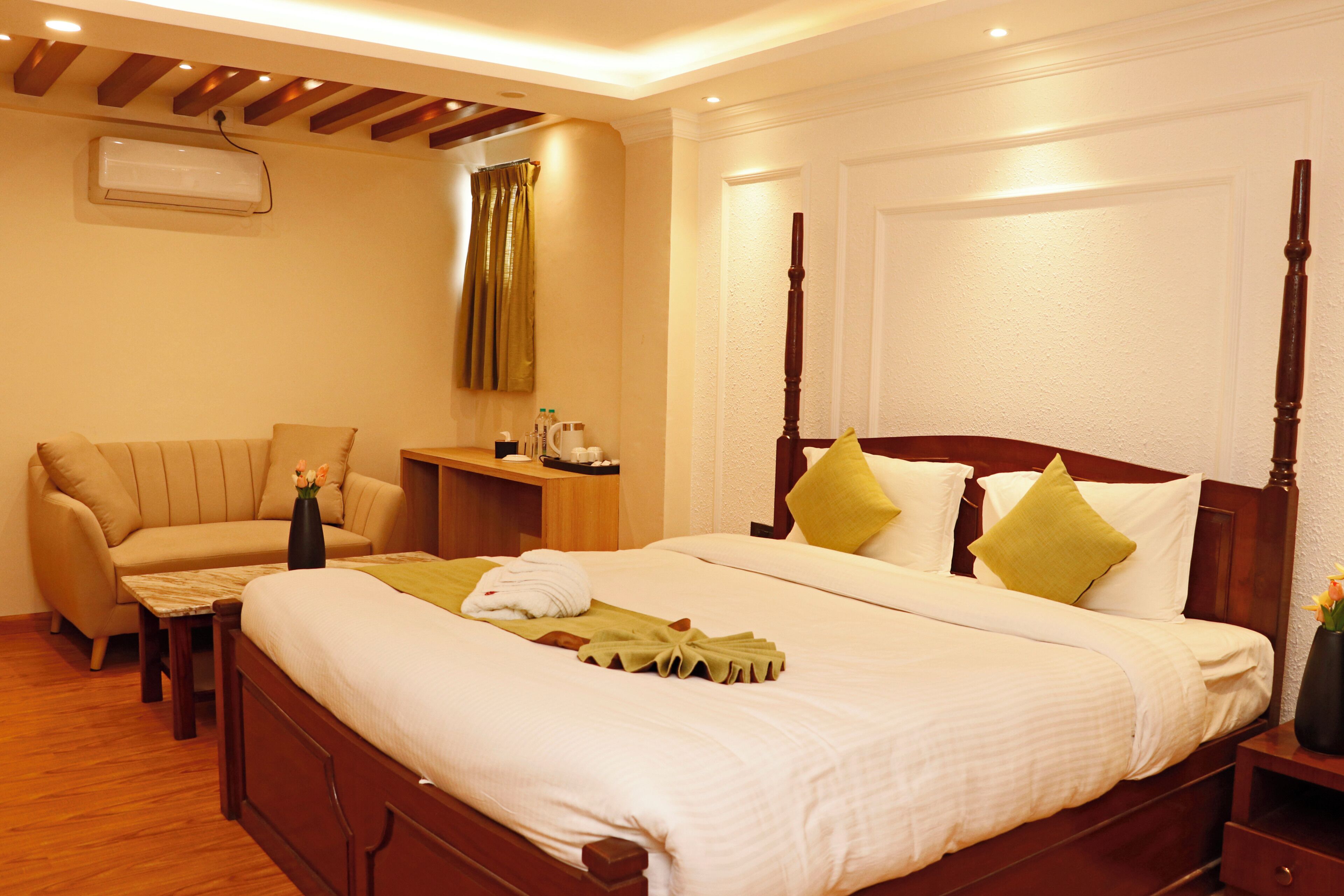 Quarto de hotel com cama de dossel, área de estar com sofá e mesa de cabeceira com comodidades.