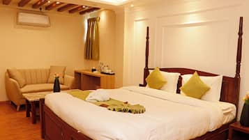 Quarto de hotel com cama de dossel, área de estar com sofá e mesa de cabeceira com comodidades.