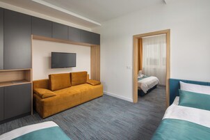 Quarto de hotel moderno com sofá, duas camas, televisão e guarda-roupa.