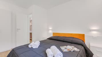 Cama bem arrumada com edredom cinza escuro e duas toalhas brancas enroladas, cabeceira de madeira e uma revista sobre a cama.