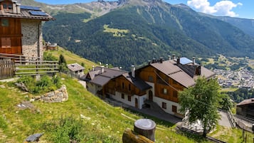 Uma aldeia de montanha com casas de madeira tradicionais, um edifício de pedra e vista para as montanhas circundantes.