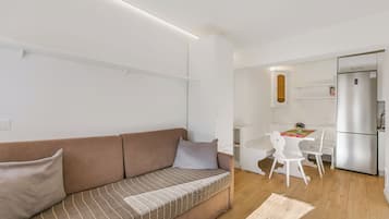 Uma sala de estar moderna com um sofá marrom, uma mesa de jantar com cadeiras e uma área de cozinha com geladeira.
