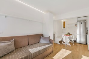 Uma sala de estar moderna com um sofá marrom, uma mesa de jantar com cadeiras e uma área de cozinha com geladeira.