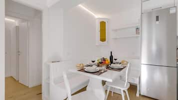 Cozinha moderna com armários brancos, geladeira embutida e mesa de jantar para quatro pessoas.
