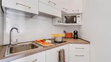Cozinha moderna com pia de aço inoxidável, micro-ondas, cafeteira e tábua de corte com legumes.