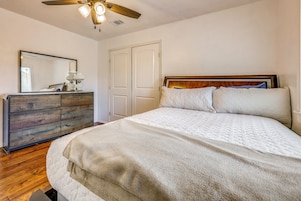 Quarto com cômoda de madeira, cama com colcha acolchoada, ventilador de teto e porta branca.