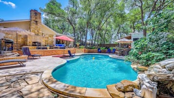 Uma piscina com borda de pedra, rodeada por espreguiçadeiras e uma área de churrasco.