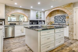 Uma cozinha moderna com ilha central, armários brancos e parede de destaque em pedra.