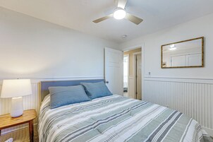 Quarto com cama, mesa de cabeceira com abajur, ventilador de teto e espelho na parede.