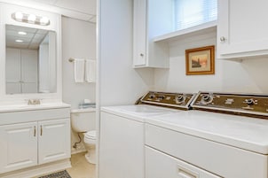Uma lavanderia com máquina de lavar, secadora e espelho sobre a pia.