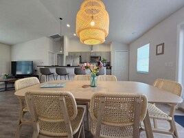 Uma sala de estar moderna com área de jantar, cozinha ao fundo e uma luminária trançada grande sobre a mesa.