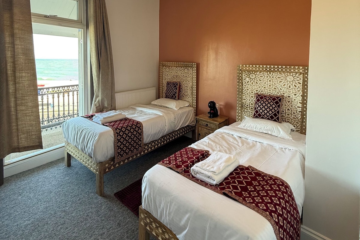 Quarto de hotel com duas camas, vista para o mar e cabeceira estampada.