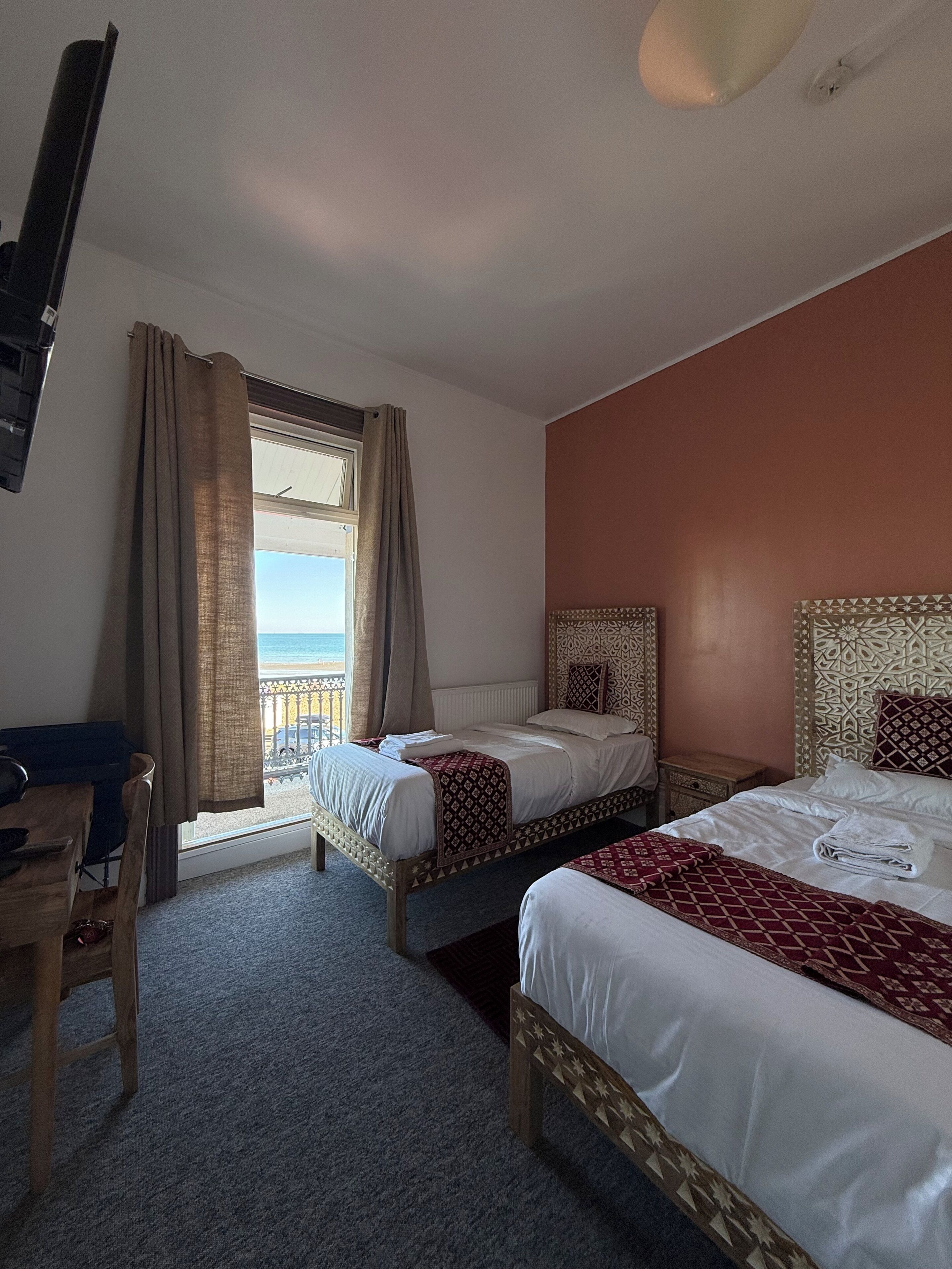 Quarto de hotel com duas camas, uma escrivaninha e vista para o mar.