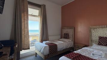 Quarto de hotel com duas camas, uma escrivaninha e vista para o mar.
